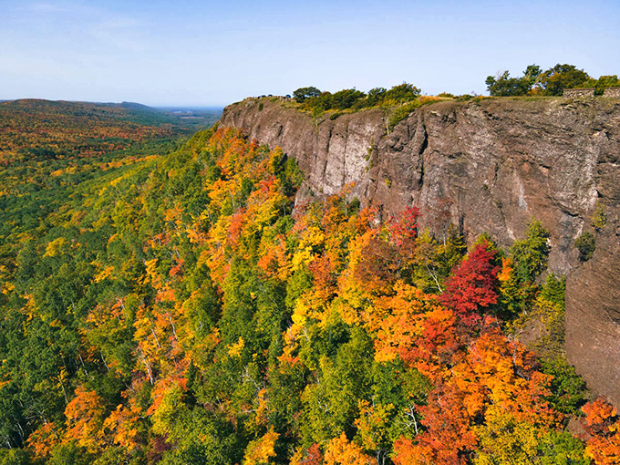 Autumn's fiery display cascades down the cliff face, creating a vertical rainbow of red, orange, and gold.