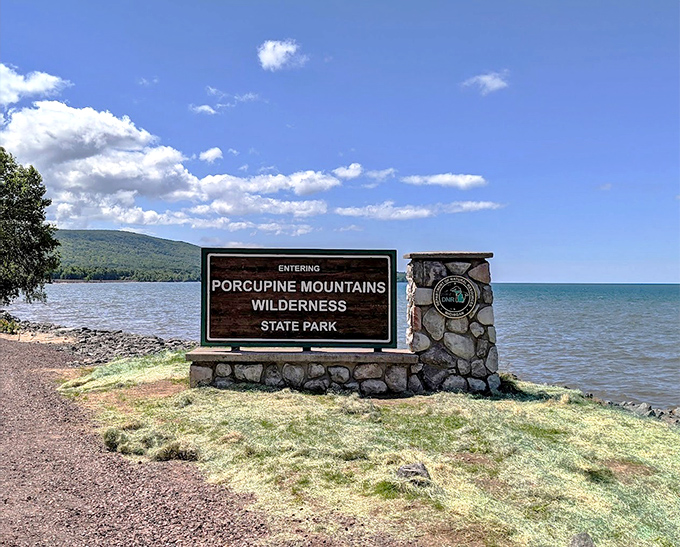 The park entrance sign stands sentinel between forest and lake, marking the threshold between ordinary life and wilderness adventure.