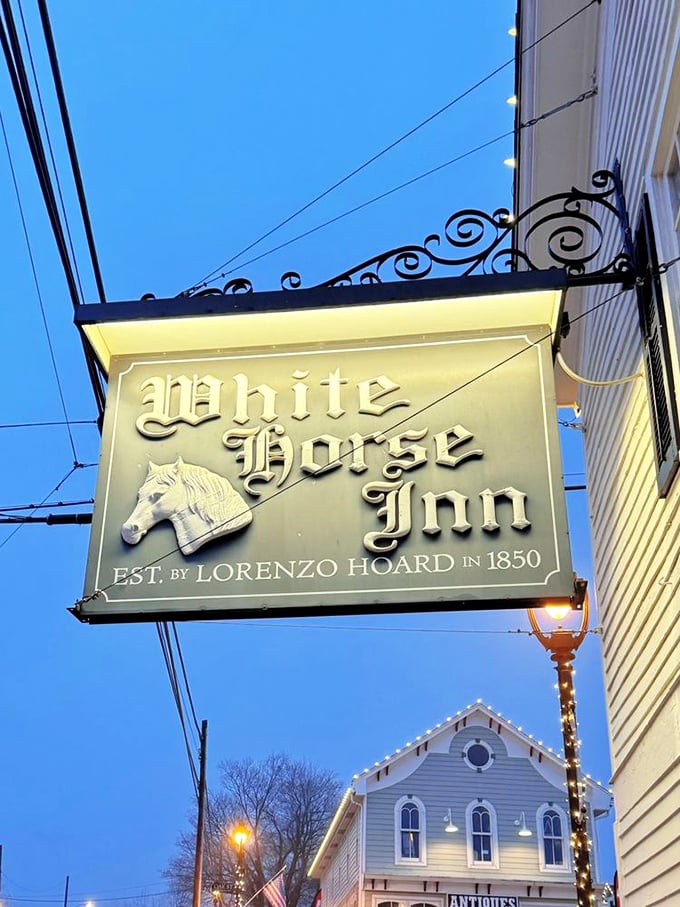 The iconic White Horse Inn sign glows invitingly against the evening sky, a beacon for hungry travelers just as it was when Lorenzo Hoard established it in 1850.