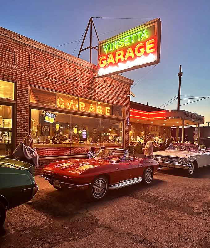 Outside: Classic cars gather at dusk beneath the glowing Vinsetta sign &ndash; a scene that captures Detroit's soul where automotive history and culinary present create perfect harmony.