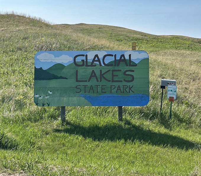 The welcoming sign stands against rolling prairie hills, a portal between everyday life and wild Minnesota beauty.