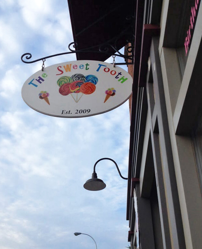 The Sweet Tooth's charming sign swings gently in the Michigan breeze, a colorful promise of the sugary wonders waiting inside.