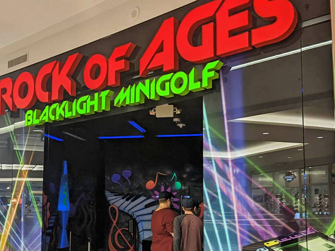 The electrifying entrance to Rock of Ages Blacklight Minigolf beckons mall-goers with its neon promise of fluorescent fun beyond the ordinary.