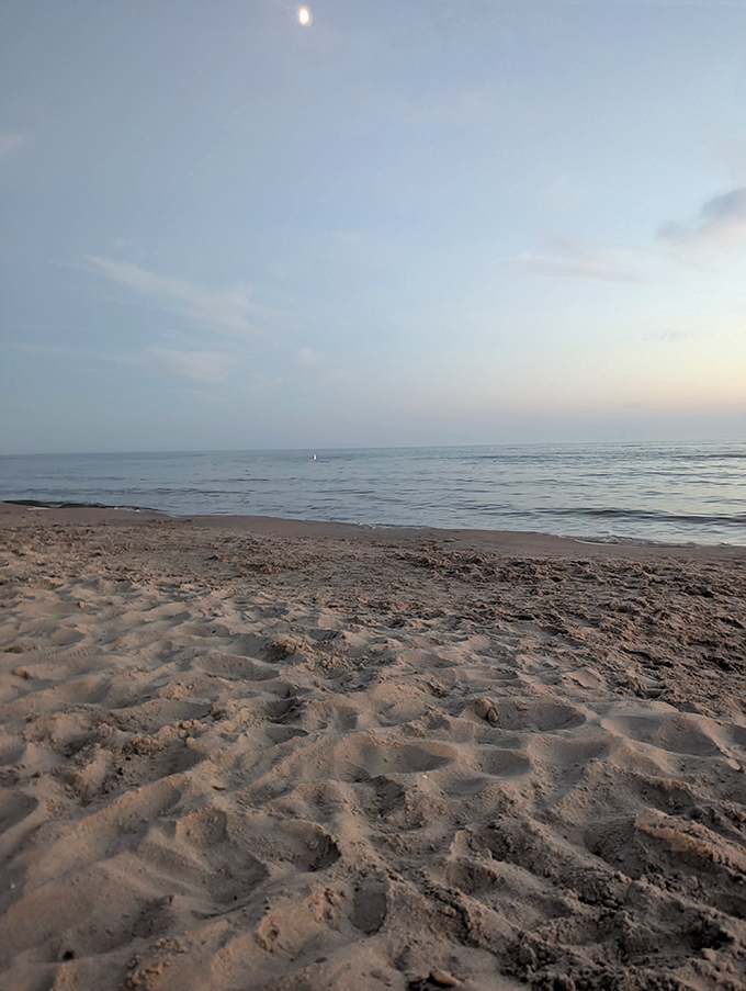 Footprints disappear into soft sand as twilight bathes the shoreline in gentle blue hues, inviting evening wanderers to leave their worries behind.
