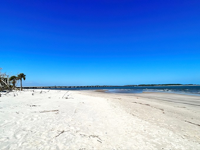 Pristine white sand stretches toward the horizon, where a distant bridge reminds you civilization exists, though you'd never know it here.