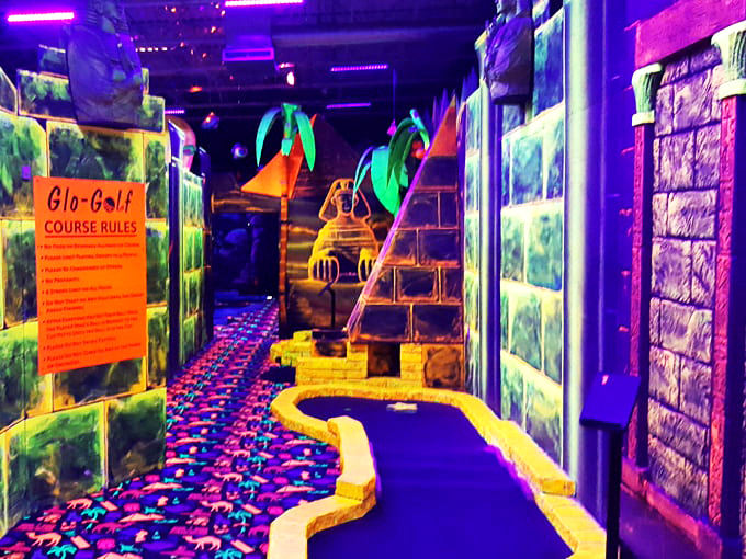 The course rules sign glows with importance, though most visitors are too mesmerized by the surrounding neon wonderland to notice.