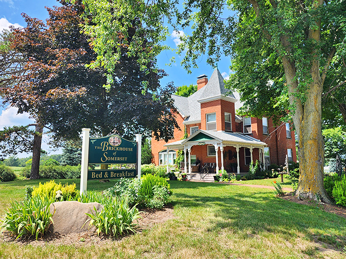 Front View: Sunlight bathes this architectural masterpiece, where intricate white porch details contrast beautifully against rich red brick, creating an irresistible welcome.