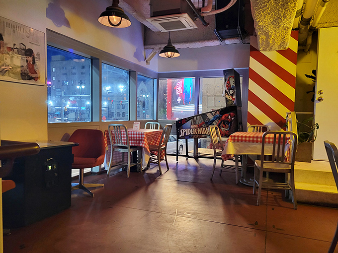 Checkered tablecloths meet industrial chic in this cozy corner, where a Spider-Man pinball machine adds playful nostalgia to the dining experience.