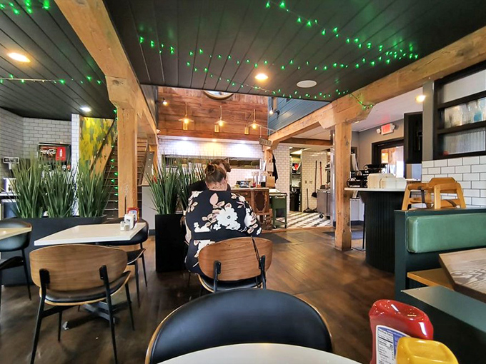 Exposed wooden beams and twinkling green lights create a cozy atmosphere where mid-century modern meets pickle chic.