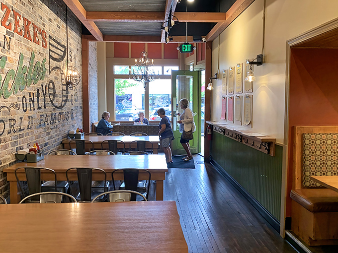 Exposed brick walls meet wooden tables in this cozy space where vintage charm and modern comfort create the perfect backdrop for serious sandwich consumption.
