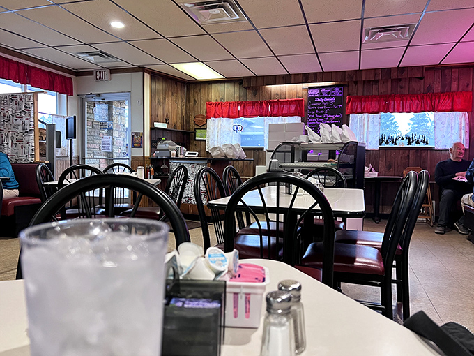 Wood paneling, red curtains, and black chairs create that perfect small-town diner atmosphere where conversations flow as freely as the coffee.