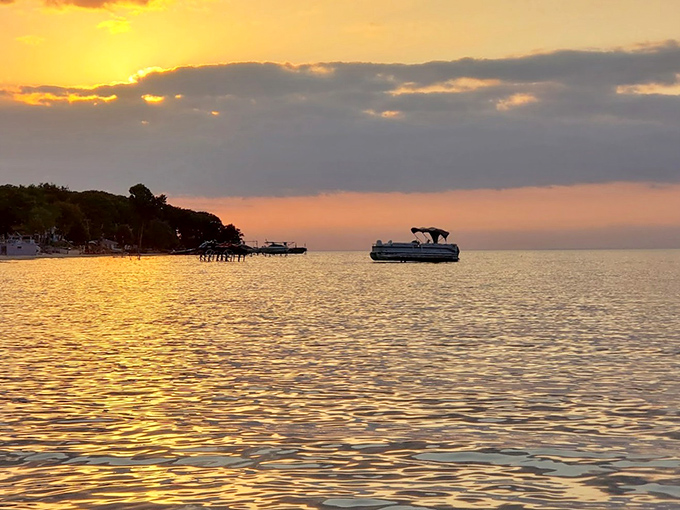Golden hour transforms Saginaw Bay into a canvas of warm hues as pontoon boats drift lazily in the distance.