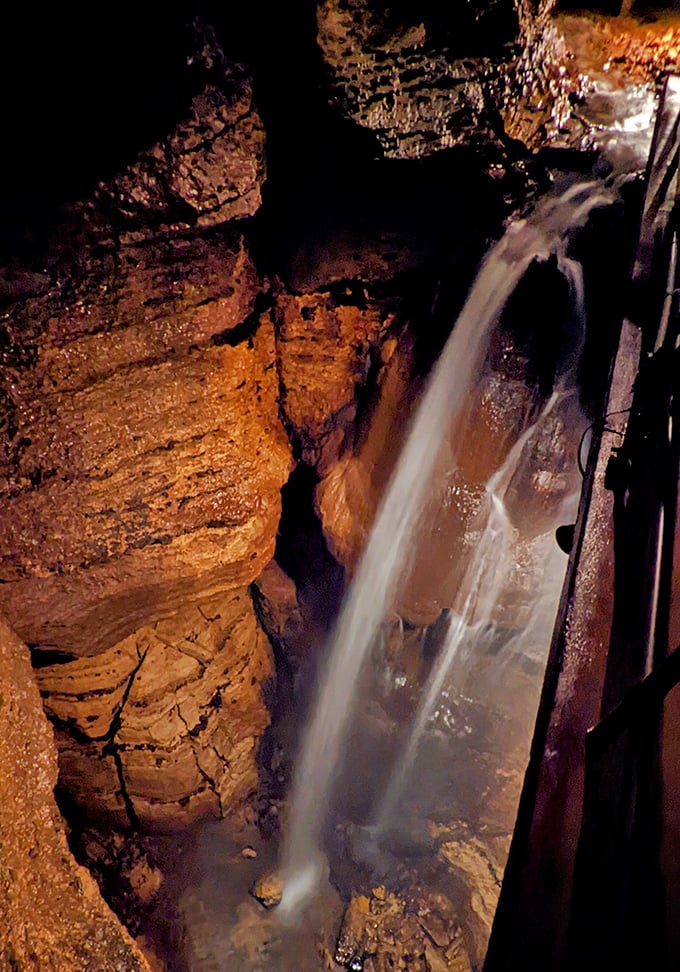 The underground waterfall cascades dramatically through the darkness, its constant flow carving the cave over countless millennia.