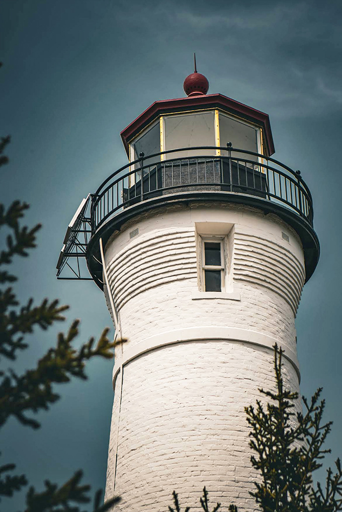 The lighthouse's distinctive red-topped lantern room creates a striking contrast against moody skies, like nature's own dramatic portrait.