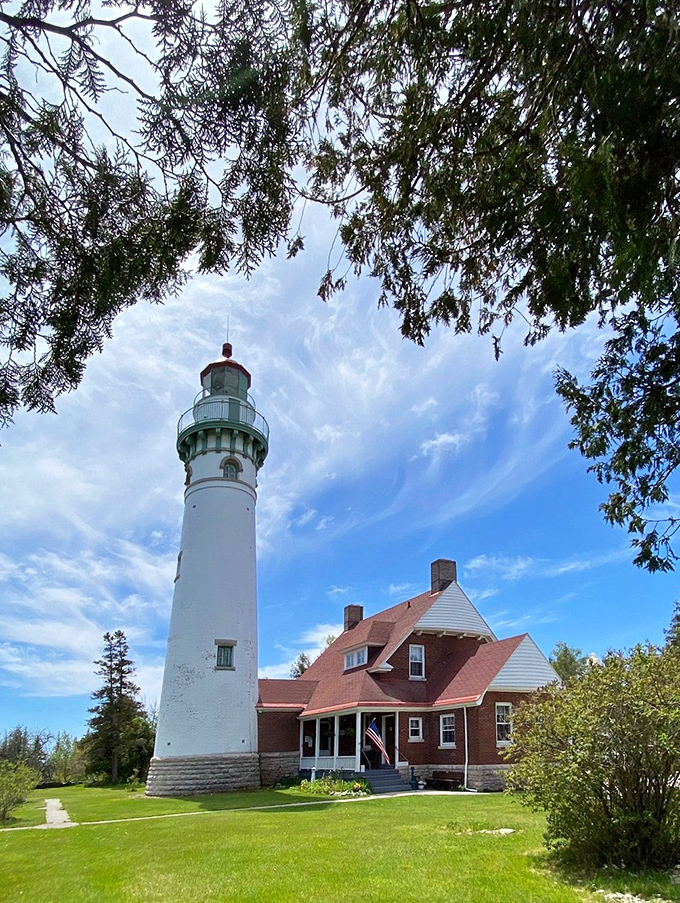 Morning light bathes the lighthouse complex, highlighting the contrast between the stark white tower and warm brick buildings nestled among evergreens.