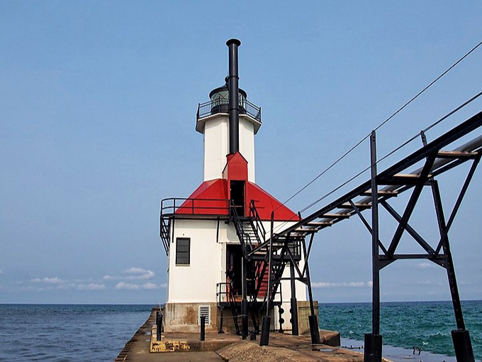 The iconic red-roofed lighthouse stands proudly against Michigan's blue sky, a cheerful maritime sentinel guarding the harbor entrance.