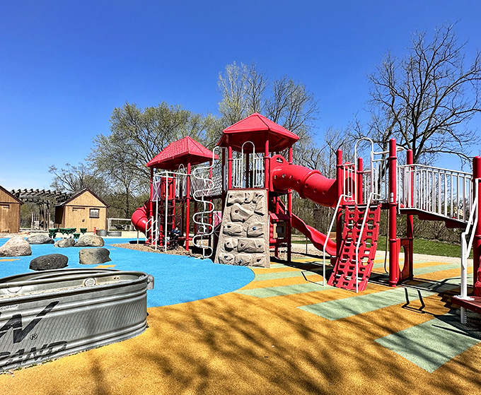 The playground's vibrant equipment pops against the blue sky, promising adventures that'll have kids sleeping soundly later. Parents, you're welcome.