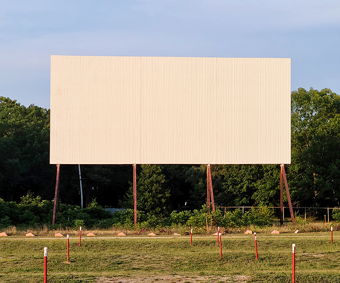 The massive screen waits silently for darkness, standing like a drive-in sentinel against the backdrop of Michigan's lush treeline.