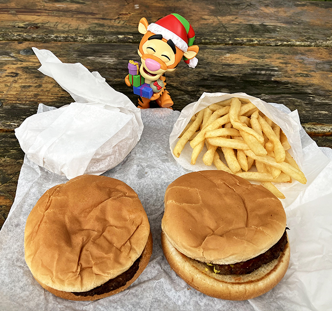 Simplicity at its finest: two perfectly proportioned burgers flanking golden fries, with a whimsical holiday figure standing guard over this feast fit for royalty.