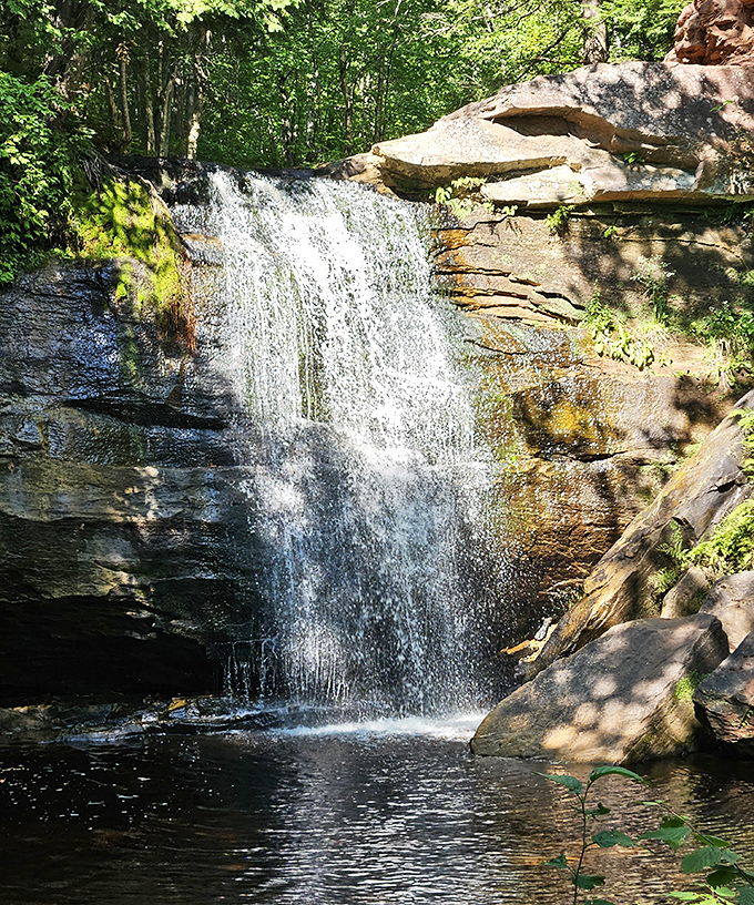 Sunlight filters through the forest canopy, illuminating this powerful cascade as it carves its eternal path through Michigan's rugged terrain.
