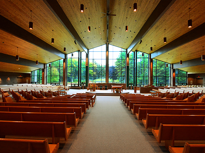Sunlight streams through floor-to-ceiling windows in this modern sanctuary, where wooden beams create a cathedral-like atmosphere among the pines.