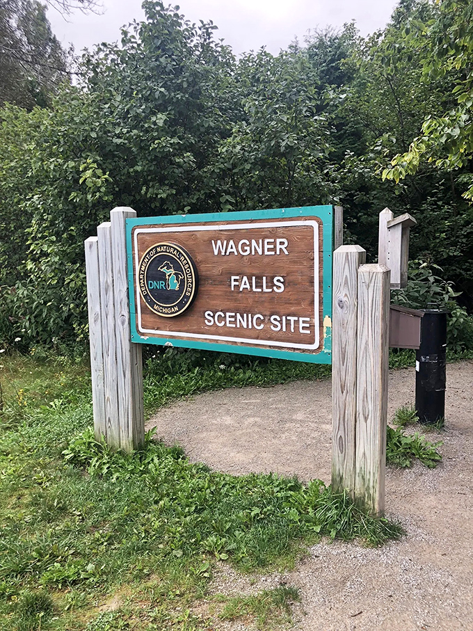The welcoming sign to Wagner Falls stands like a humble doorman, never hinting at the spectacular show waiting just beyond.