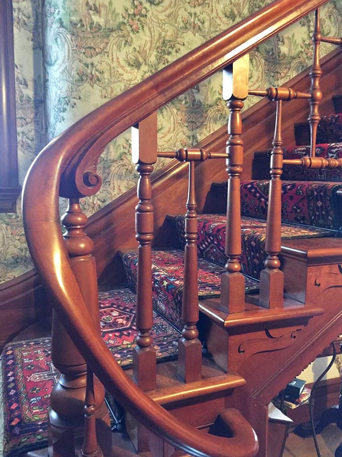 The grand wooden staircase curves gracefully upward, its polished banister telling stories of a century's worth of hands gliding along its surface.