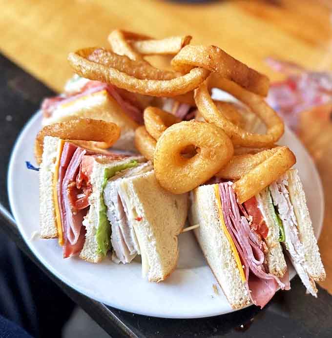 This isn't just a sandwich &ndash; it's architecture on a plate! Layers of deli meats and cheese crowned with golden onion rings that crunch like autumn leaves.