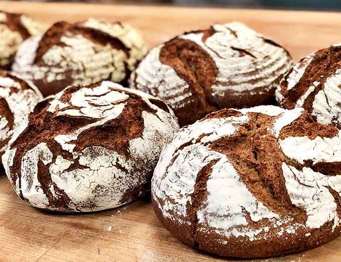 Dark, rustic loaves with crackling crusts that shatter satisfyingly when sliced, revealing the open, airy crumb that only proper fermentation can achieve.