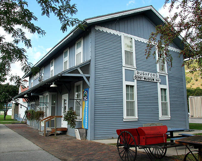 The blue-painted Rushford Depot Museum whispers tales of railroad days, complete with a charming red wagon that's seen more history than most textbooks.