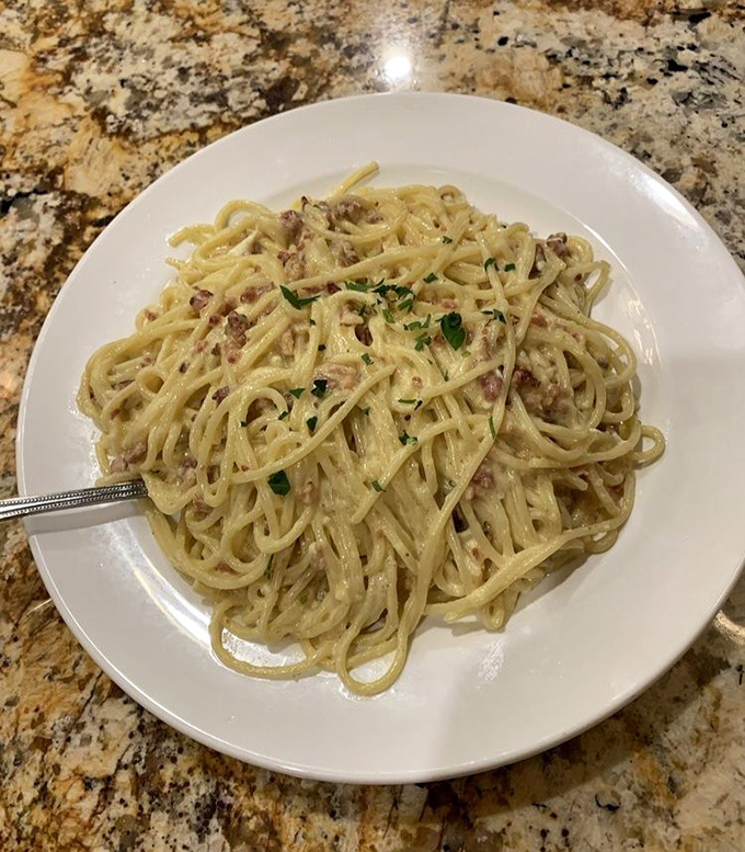 Spaghetti Carbonara arrives as a silky masterpiece – each strand perfectly coated in a rich egg sauce studded with pancetta and black pepper.