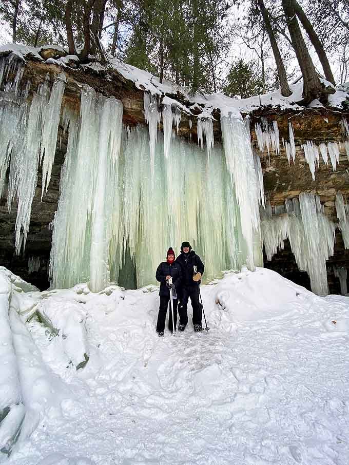 Bundled-up adventurers gather beneath towering ice formations, their colorful winter gear popping against nature's frosty palette.