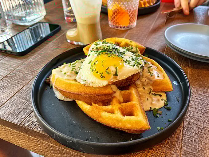 Golden waffles cradle a perfectly fried egg, the savory sauce pooling around crisp edges &ndash; breakfast elevated to an art form.