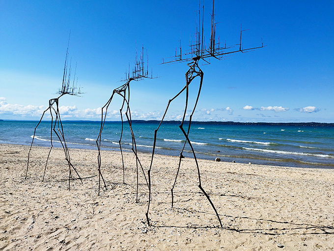 "Walkers" stride across the shoreline like alien visitors, their antenna-topped forms creating otherworldly silhouettes against Michigan's waters.