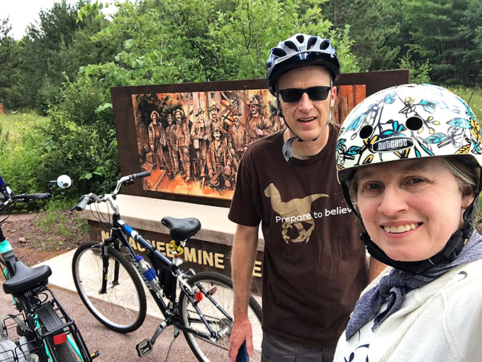 Cyclists pause at the Negaunee Mine Memorial, where rusted tributes to underground heroes remind us some treasures came at tremendous cost.