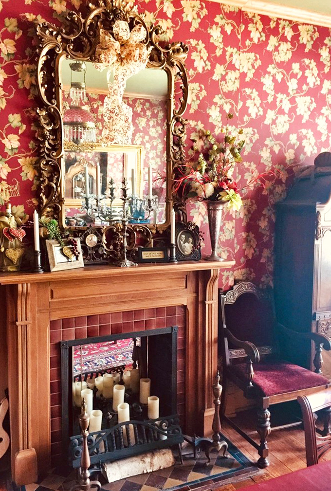 A parlor fireplace framed by rich woodwork, with ornate mirror above &ndash; the perfect spot for evening conversations and quiet contemplation.