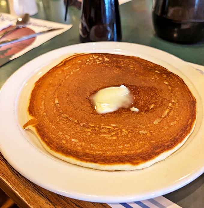 A perfect golden pancake that extends beyond its plate, crowned with a slowly melting pat of butter - breakfast royalty.