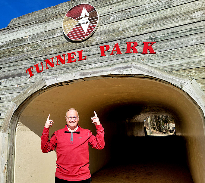 A visitor celebrates the simple joy of discovery at Tunnel Park's entrance, where adventure awaits beyond the archway.