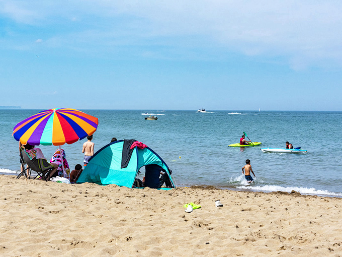 Beach tents and colorful umbrellas dot the landscape as water enthusiasts enjoy paddleboarding on Lake Michigan's surprisingly clear waters.