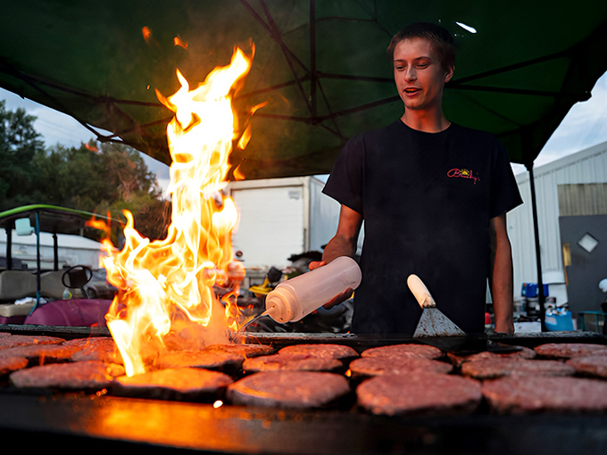 Flames leap dramatically as a grill master tends to dozens of sizzling patties, creating that irresistible aroma that follows you through dreams.