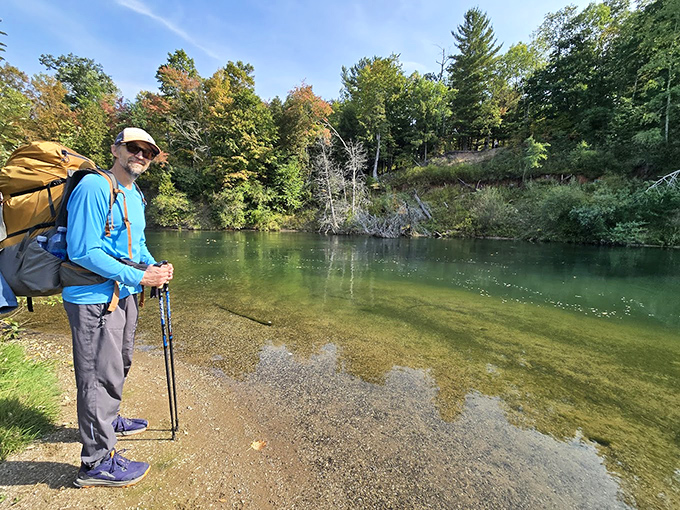 A hiker pauses at the emerald waters of the Manistee River, contemplating whether that backpack was really necessary for such pristine views.