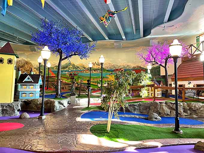 The whimsical indoor mini-golf course features colorful trees, charming buildings, and playful lighting that delights guests of all ages.