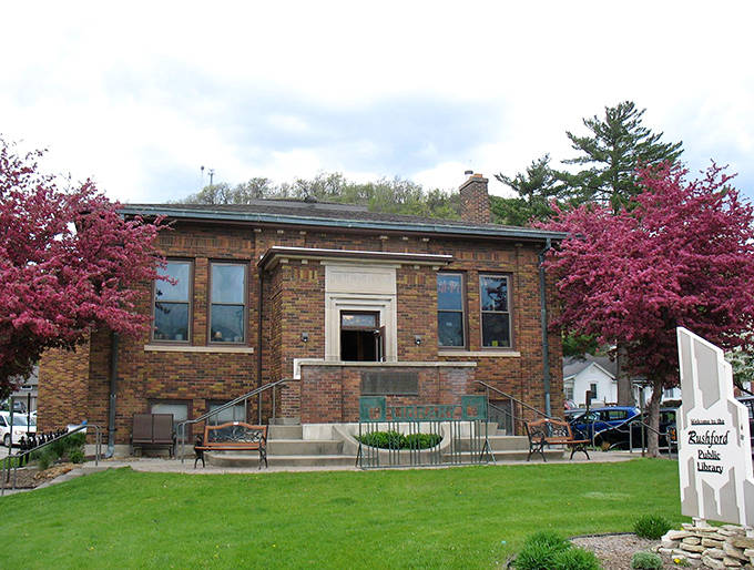 Rushford's Public Library blooms between flowering trees, a brick sanctuary of stories where three generations often browse books together.
