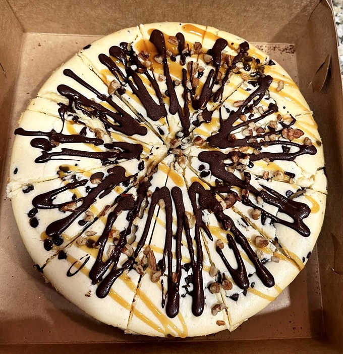 Chocolate drizzle cascades over vanilla cheesecake like a Jackson Pollock painting you can eat, topped with crunchy pecans for textural contrast.
