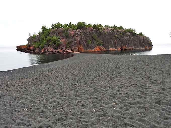 Where dark meets light: The volcanic-like sand creates a dramatic runway leading to the imposing cliff peninsula.