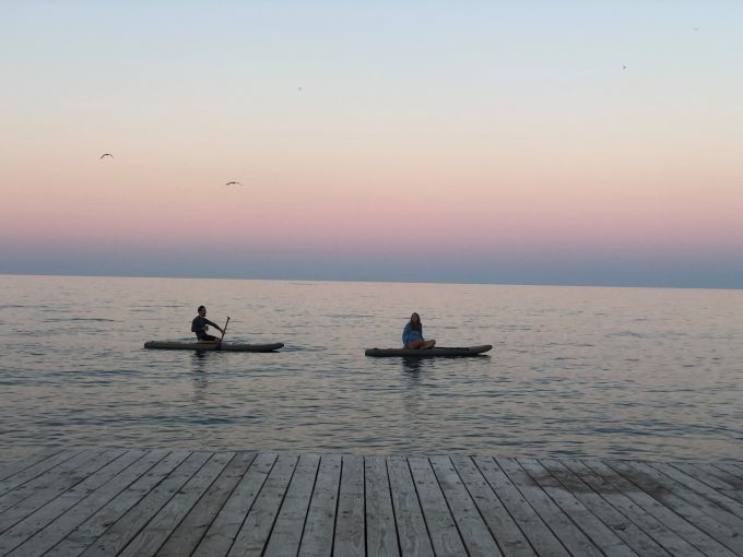 Sunset paddleboarders glide across Lake Huron's glass-like surface, chasing the last golden rays of day.