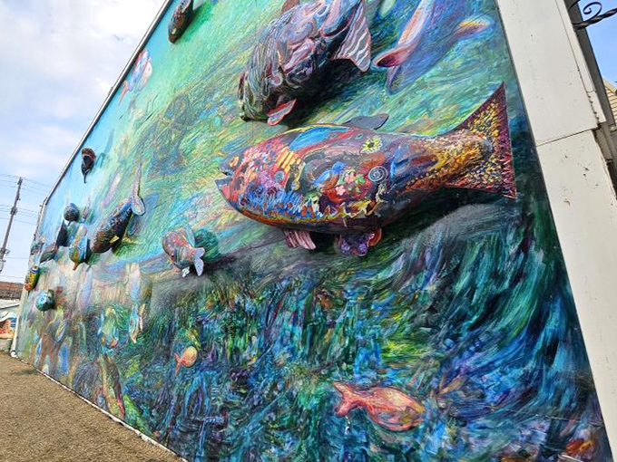 The low angle highlights how the sculptural fish create actual shadows across the painted background, blurring the line between art and reality.