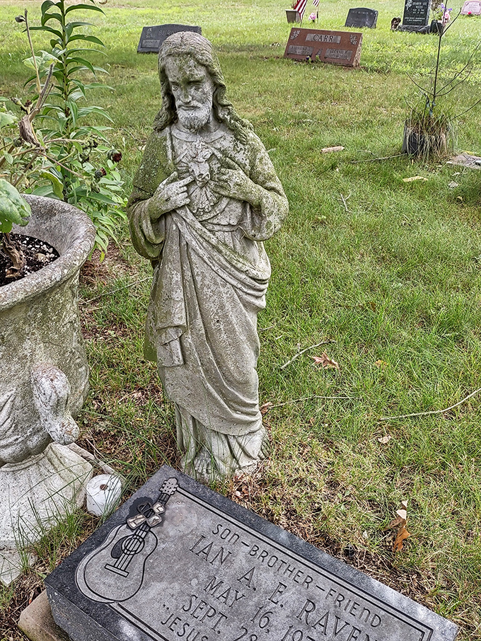 A moss-kissed statue stands in quiet contemplation, its weathered features softened by time yet still conveying profound spiritual comfort to cemetery visitors.