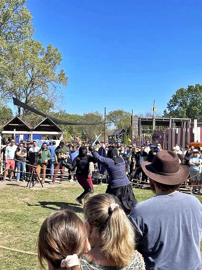 Visitors gather around an outdoor stage where performers demonstrate historical combat techniques with equal parts educational value and theatrical flair.