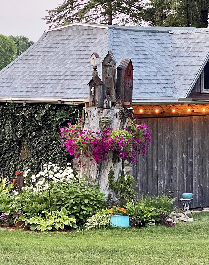 Whimsical garden art perches atop a tree stump, surrounded by vibrant flowers &ndash; proof that Victorian sensibilities included a healthy dose of playfulness.